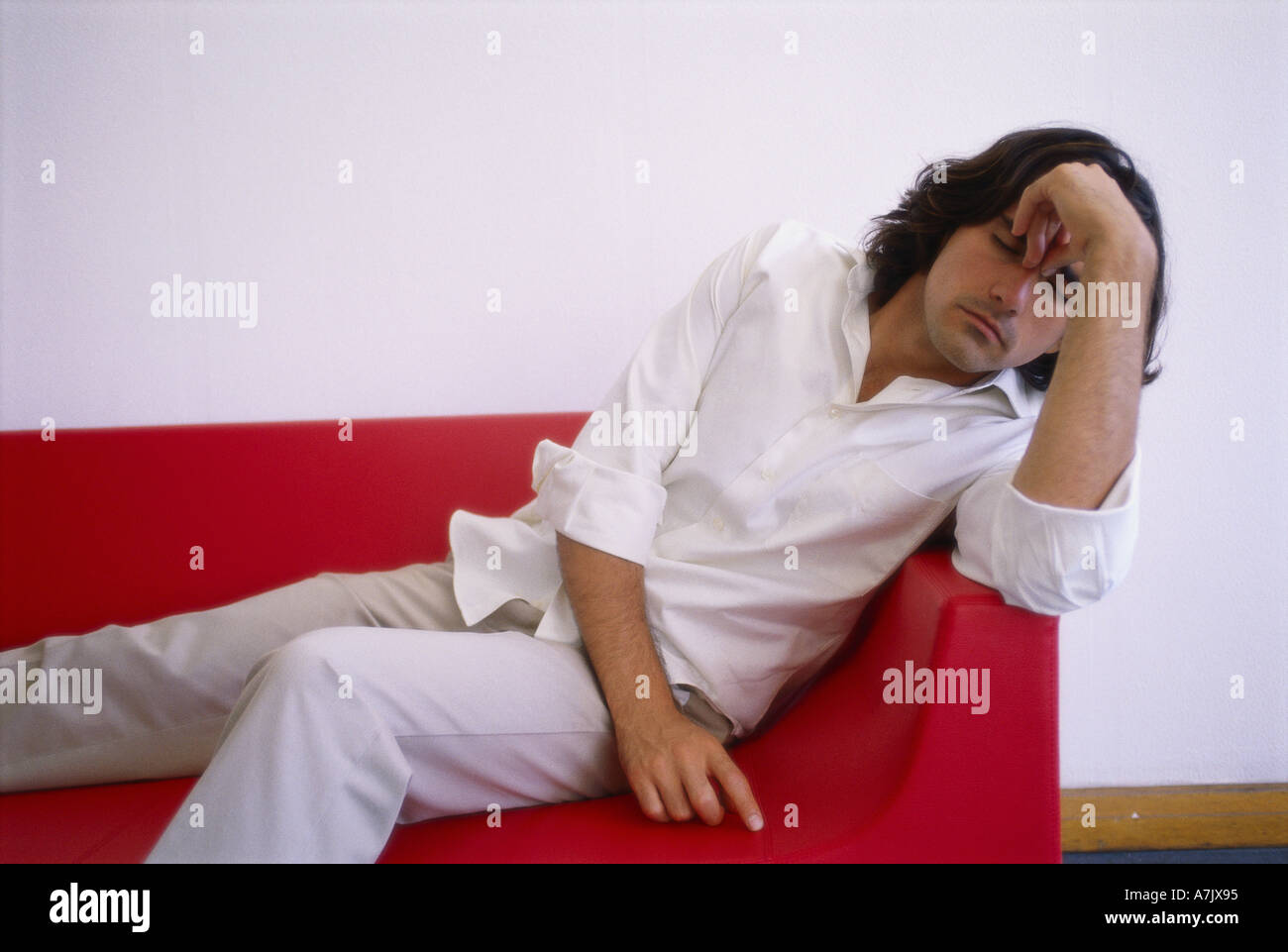 Young man reclining on a couch with his hand on his head Stock Photo ...