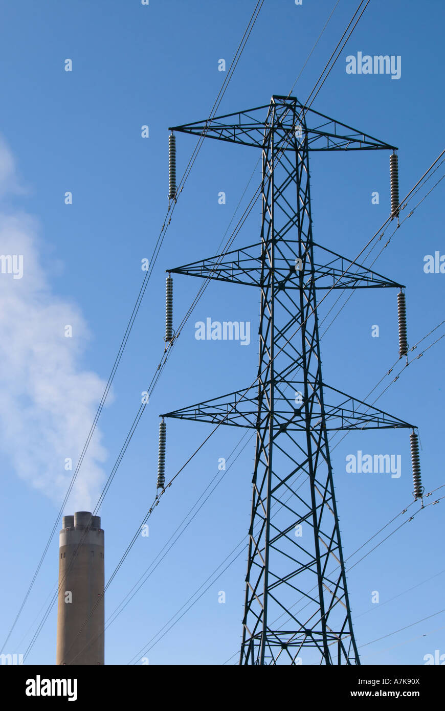 A smoking power station chimney stack and electricity pylon on a plain ...