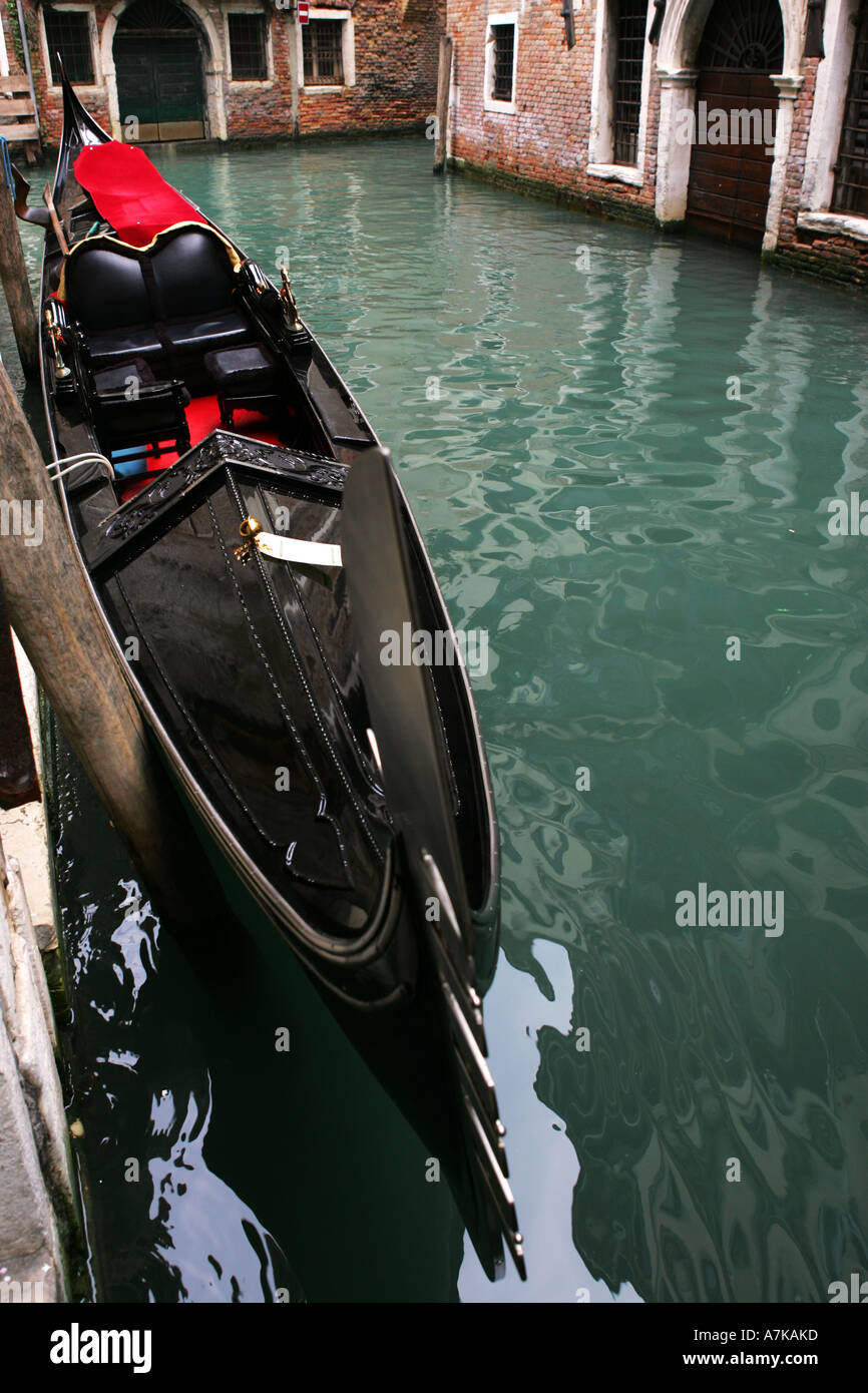 Black Venetian gondola contrasts with emerald green canal and pink ...