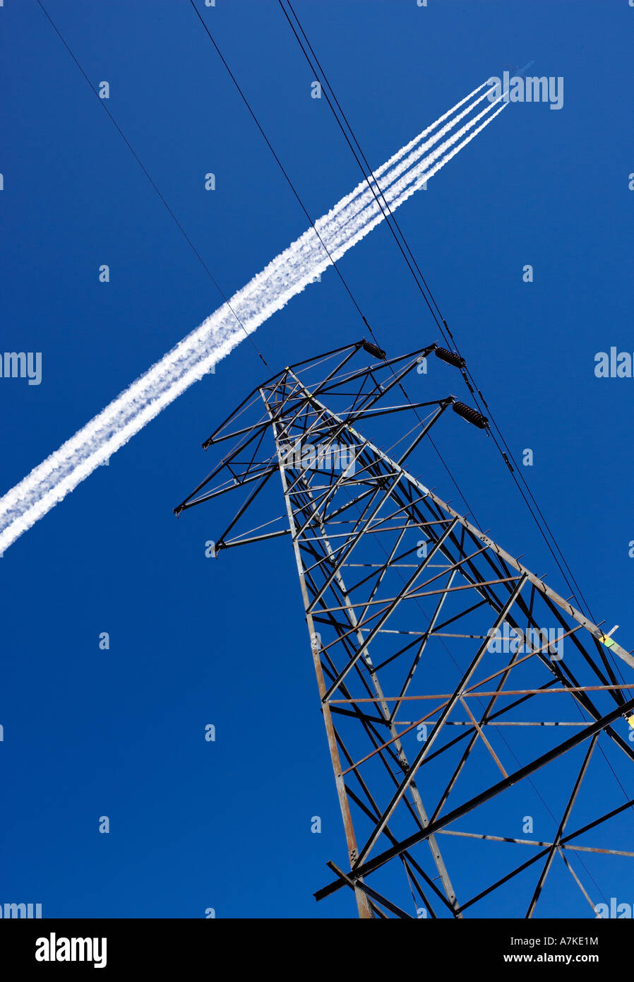 ELECTRICITY PYLON AND CABLES WITH JET AIRCRAFT EXHAUST TRAIL IN BLUE ...