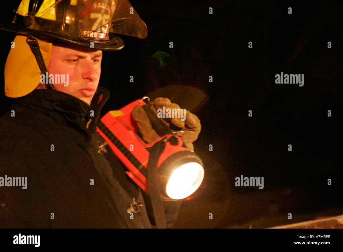 A fire fighter with a flashlight looking for a victim in a structure ...