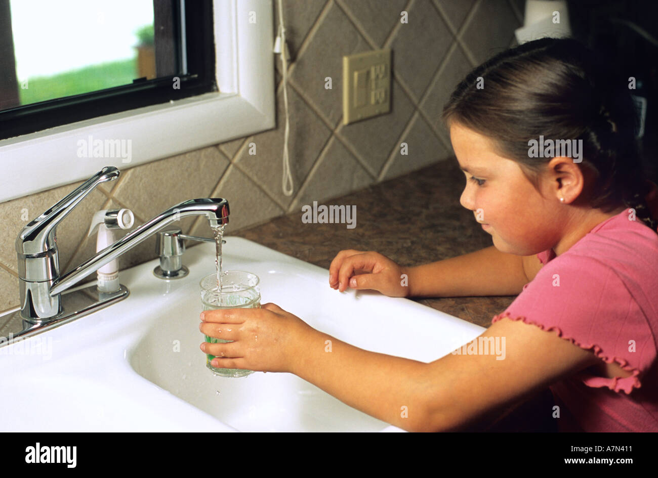 Eight year old girl getting a glass of water from the kitchen faucet ...