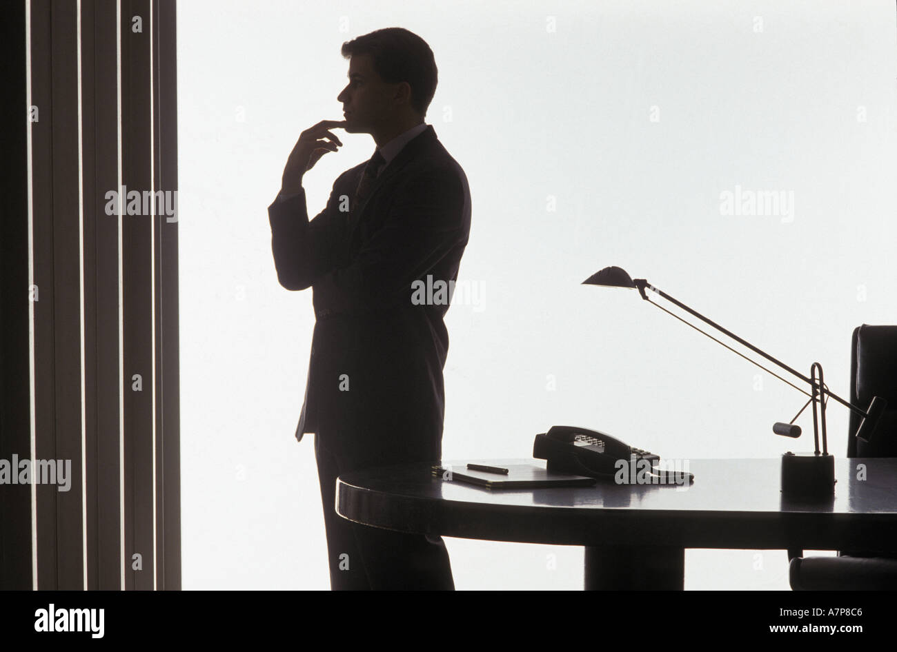 Contemplative male executive standing next to desk Stock Photo - Alamy