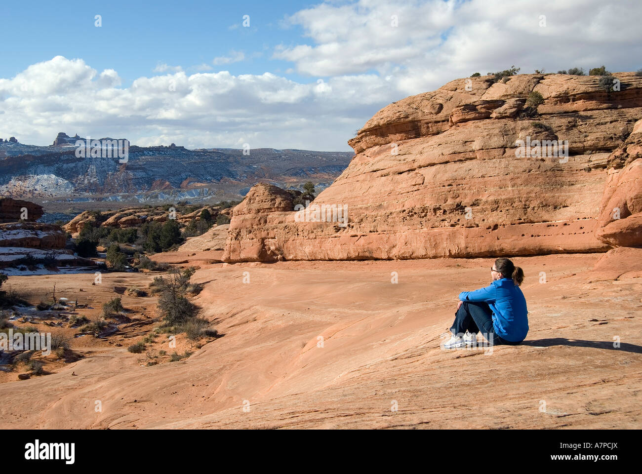 Young woman sitting on Entrada sandstone ledge and enjoying view Arches ...