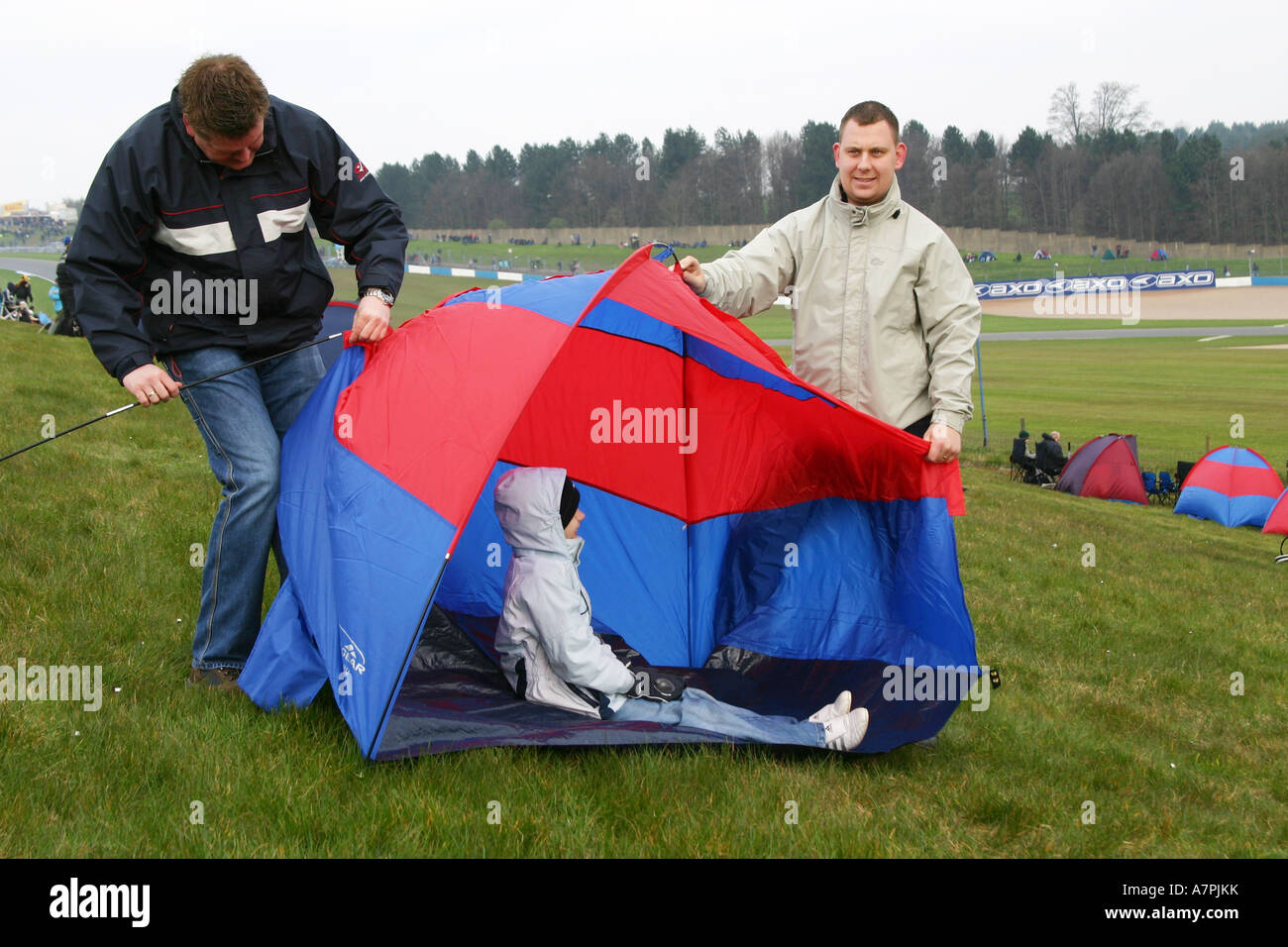 Two men erecting tent type shelter with small child already sitting ...