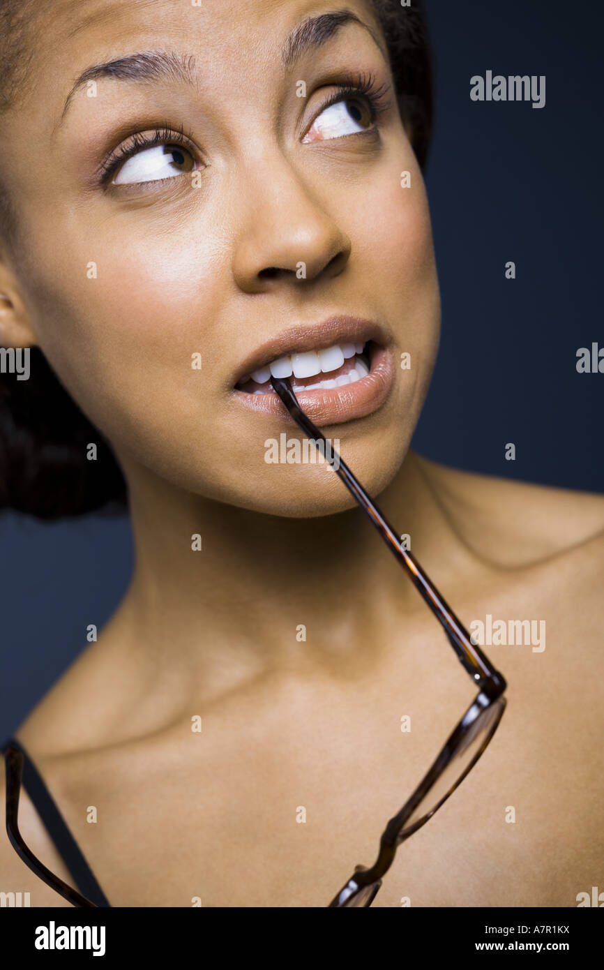 Woman looking up biting arm of eyeglasses Stock Photo - Alamy