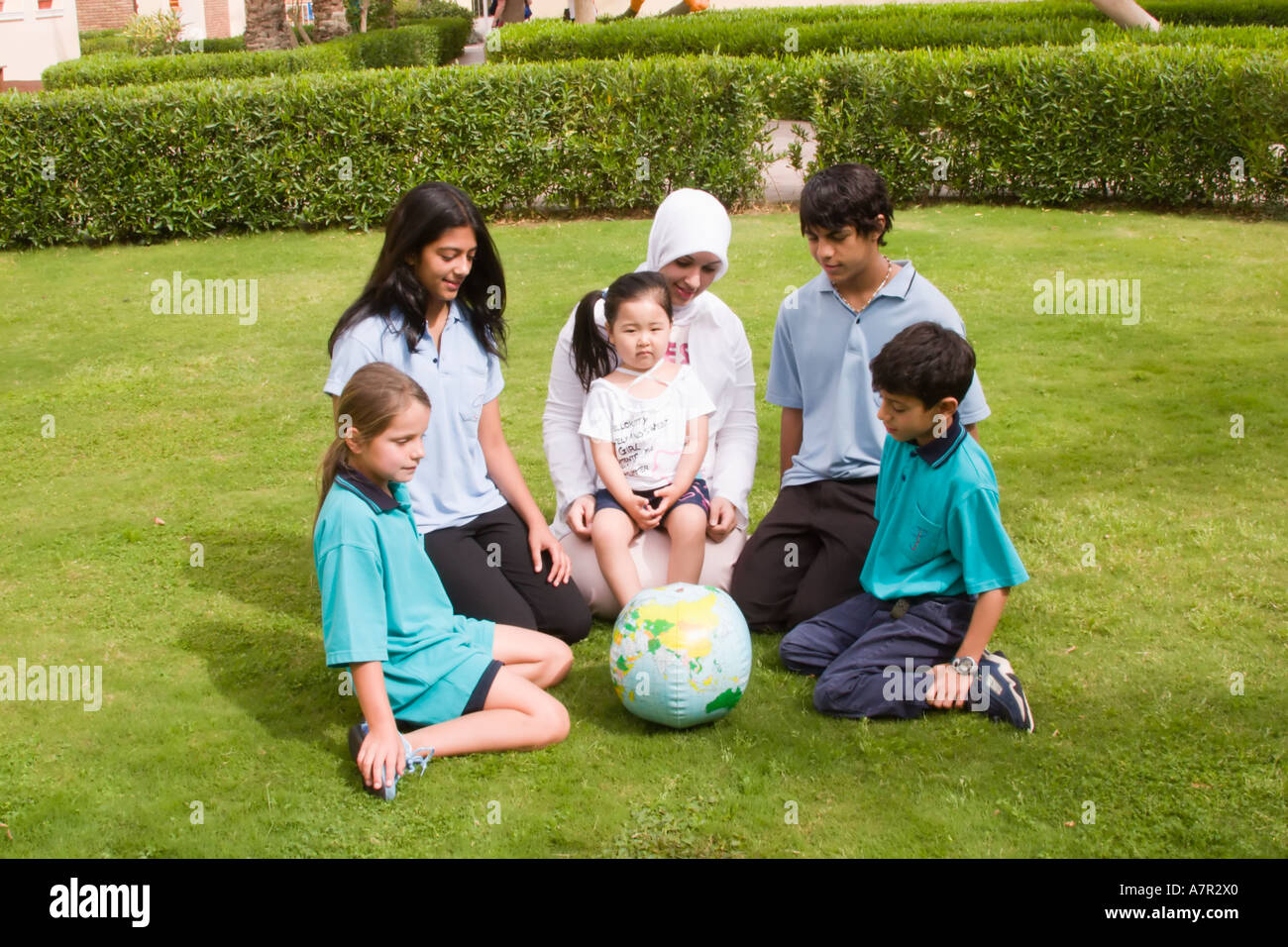 school children sitting outside on grass looking at globe of earth ...