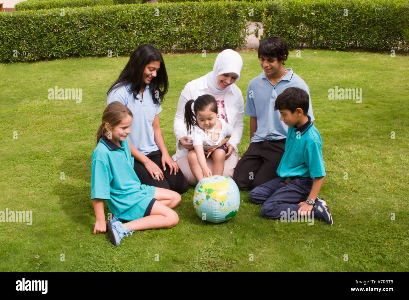 school children sitting outside on grass looking at globe of earth ...