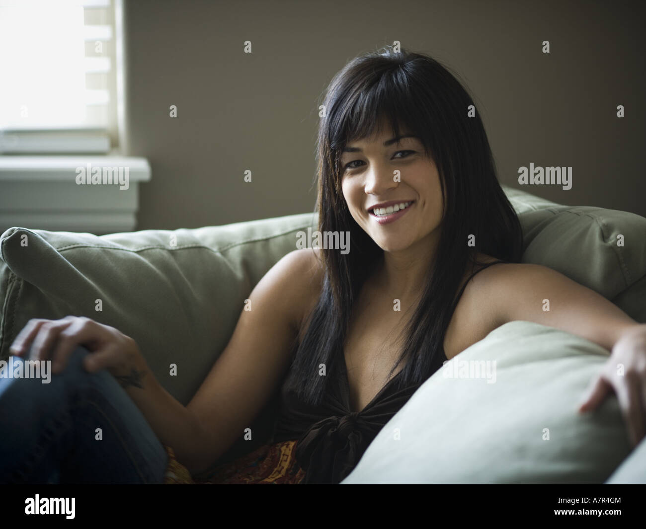 Woman sitting on sofa smiling Stock Photo - Alamy