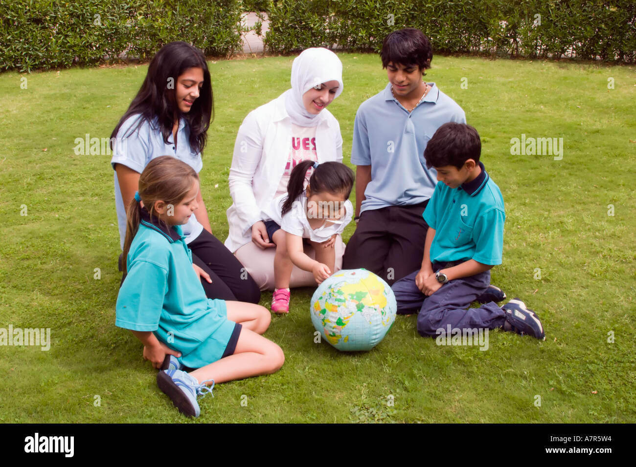 school children sitting outside on grass looking at globe of earth ...