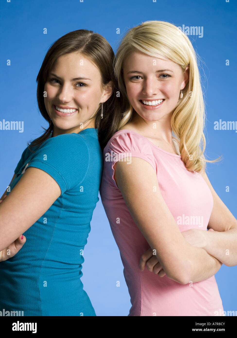 Two girls with arms crossed back to back smiling Stock Photo - Alamy