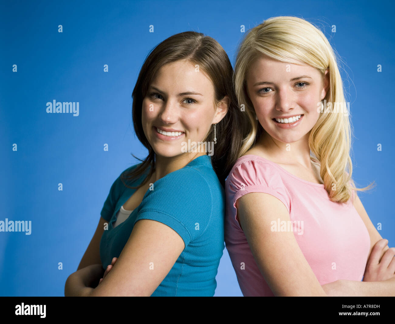 Two girls with arms crossed back to back smiling Stock Photo - Alamy