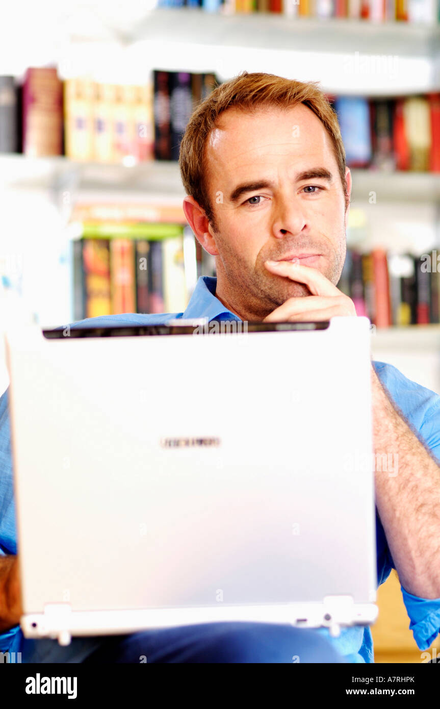 Mid adult man holding laptop and thinking Stock Photo - Alamy