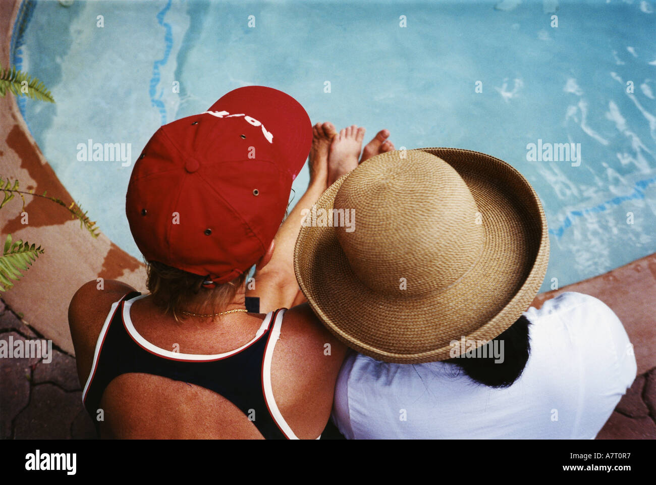 Two women with hats sitting by the swimming pool Stock Photo - Alamy