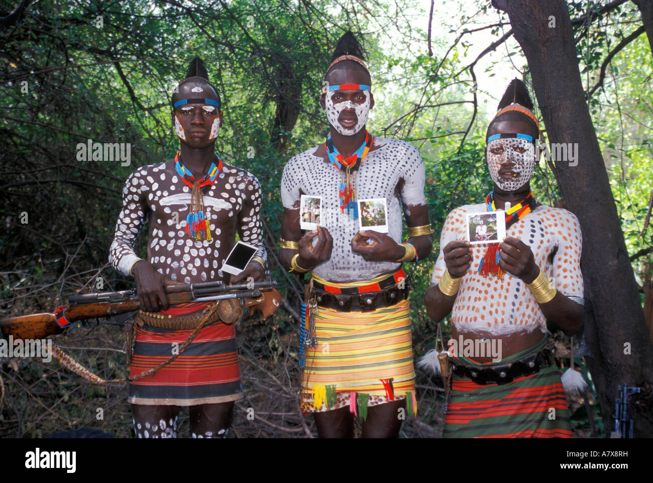 Three painted Karo warriors holding Polaroid instant photographs of ...
