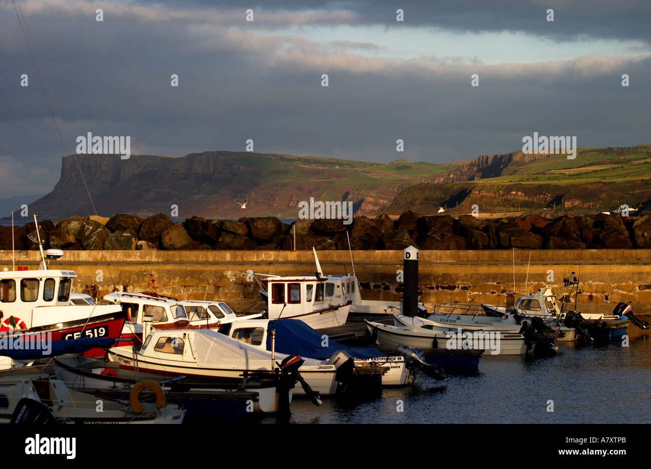 Boats in Ballycastle marina with the setting sunlight over the antrim ...