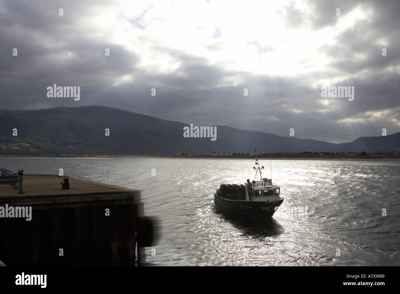 fishing boat floating off waterfoot pier in red bay under a dark cloudy ...