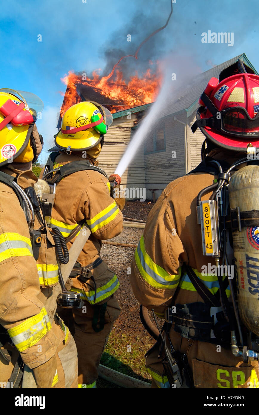 Three firefighters use a powerful hose to blast water onto the ...