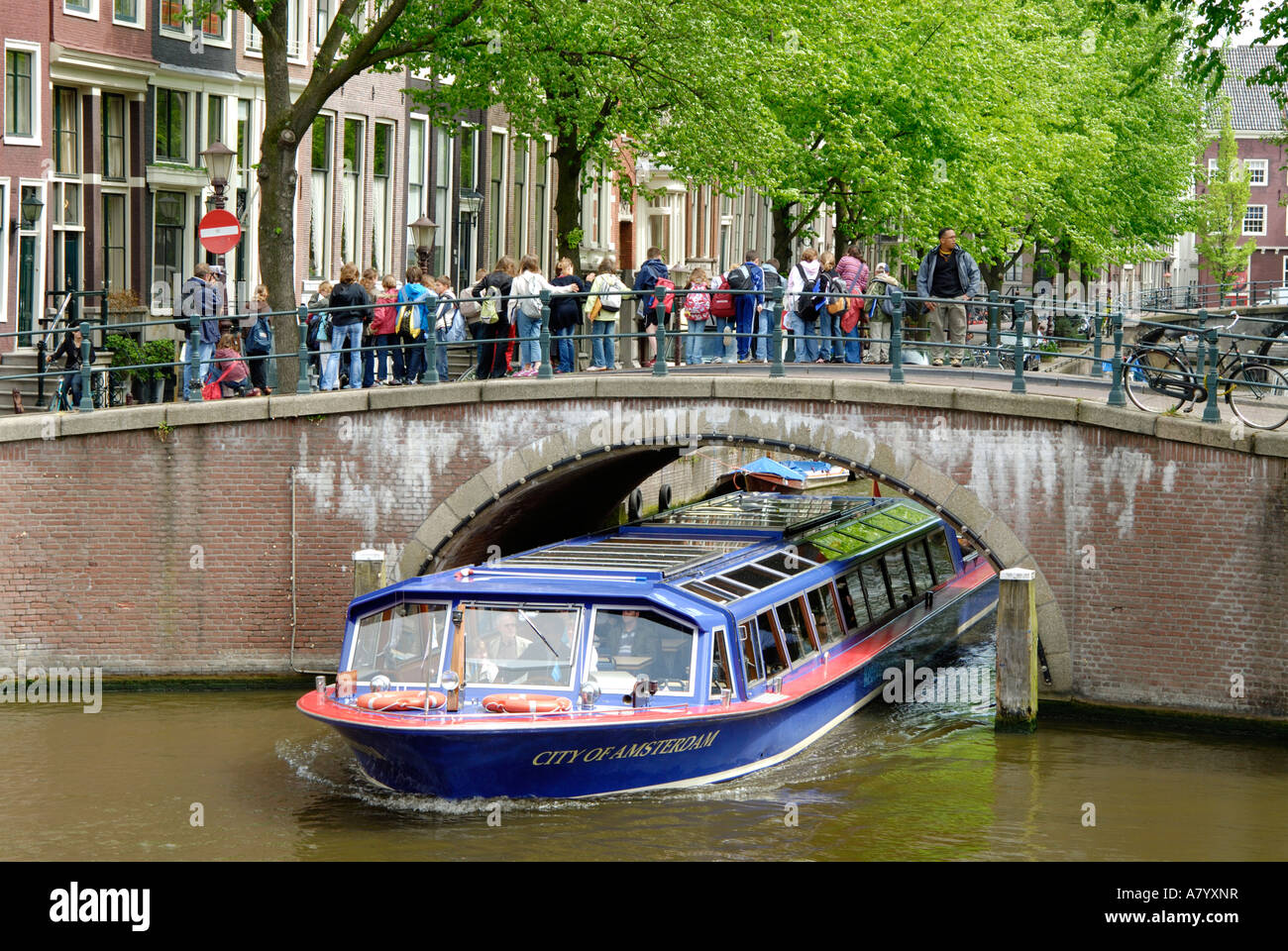 A canal tour boat in Amsterdam passes under a stone bridge, watched by ...