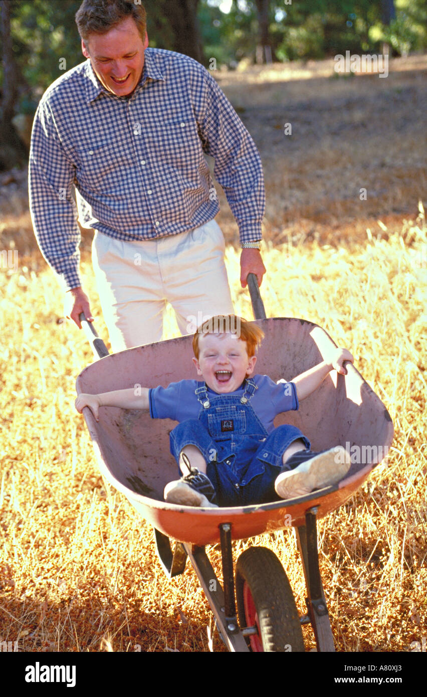 father pushing his son sitting in a wheel barrow Stock Photo - Alamy