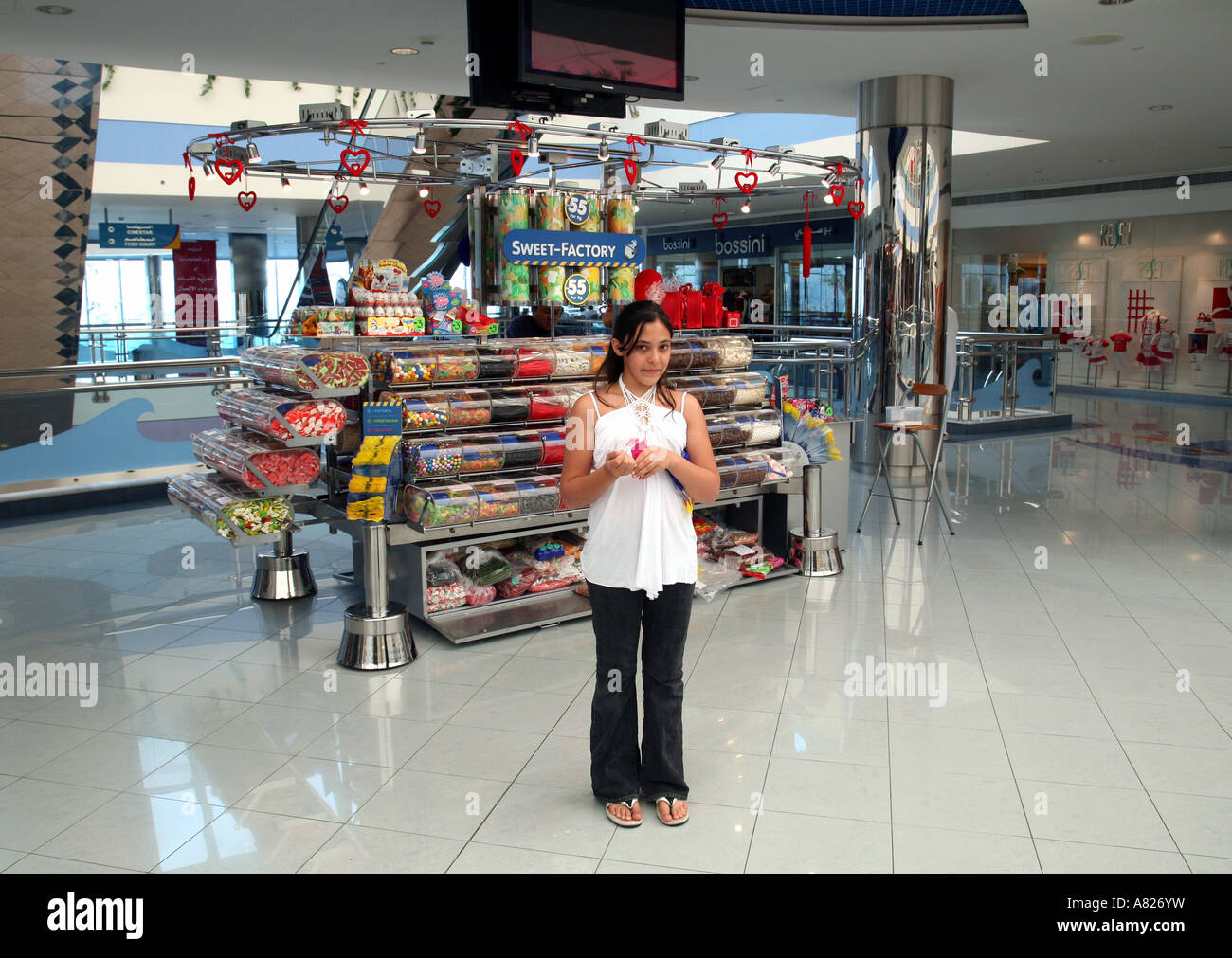 A young girl eats sweets in front of a sweet stall, Abu Dhabi Mall, Abu ...