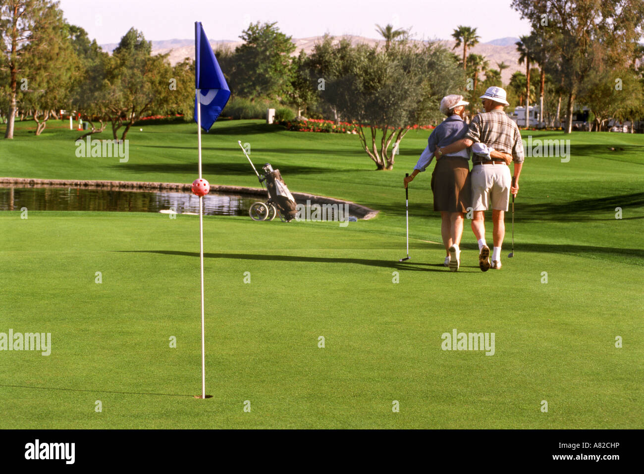 Senior couple in 70's walking off putting green together on golf course ...