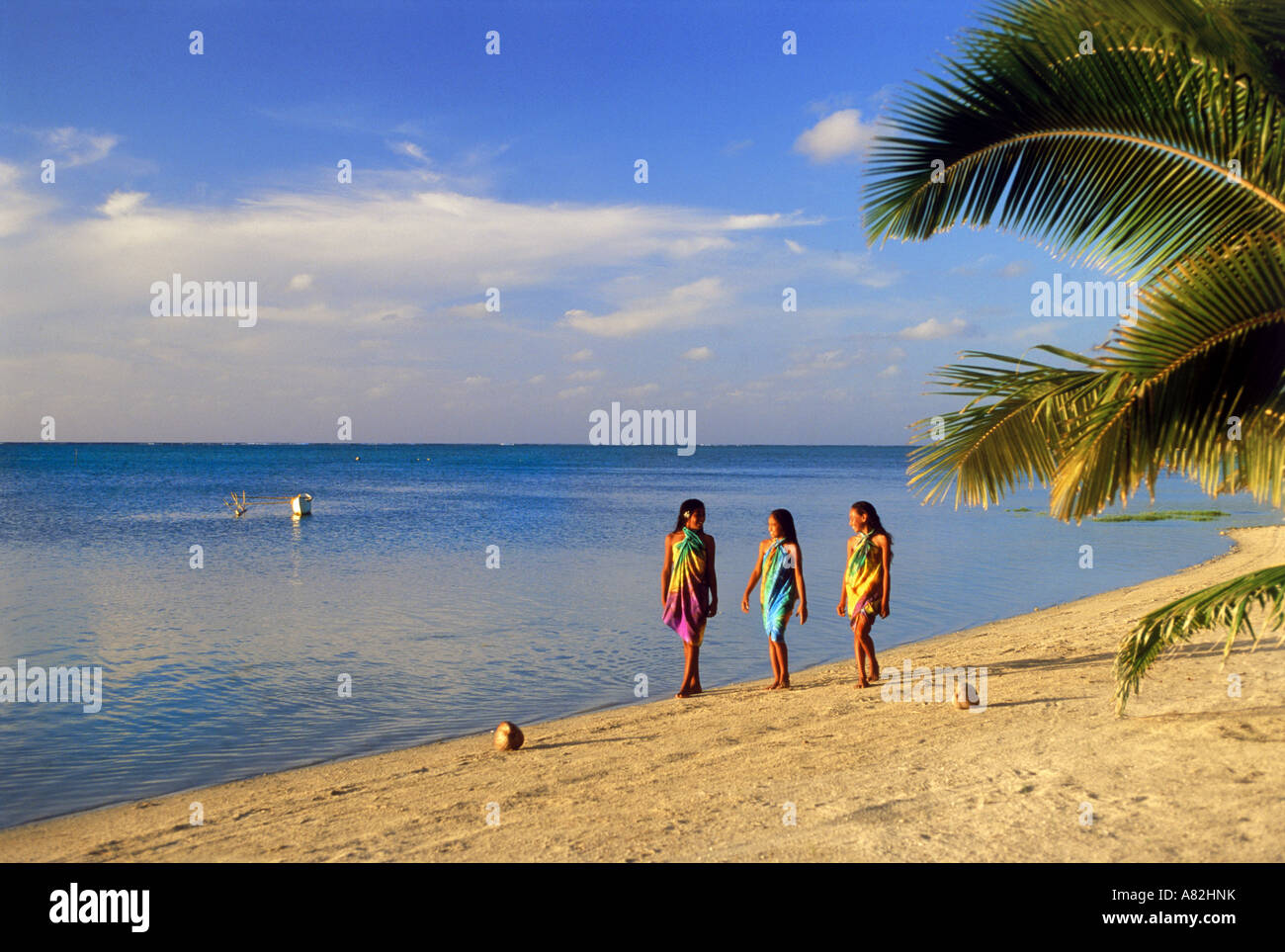Three Polynesian girls walking along sandy shore on Aitutaki Island in ...