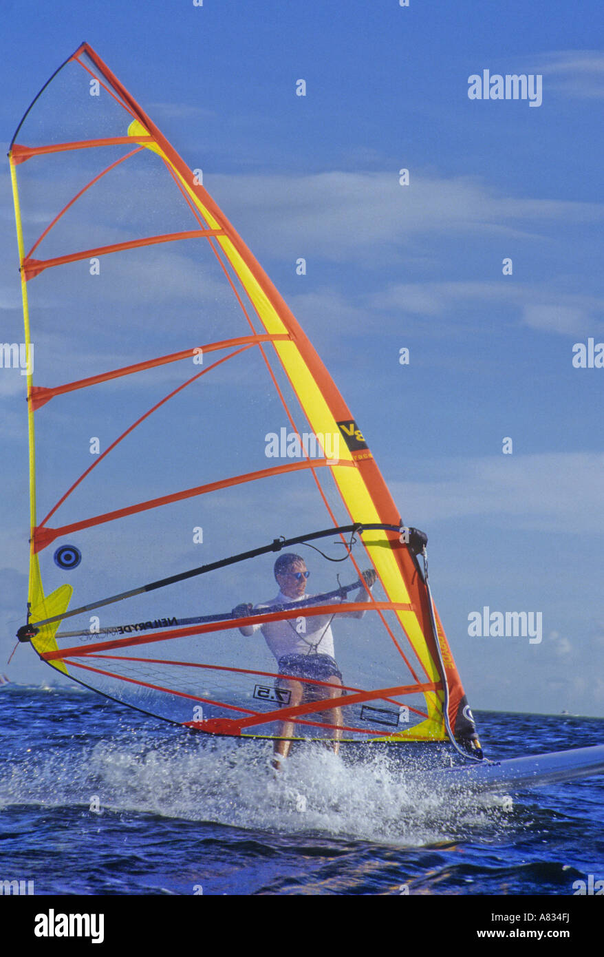 A windsurfer with a bright yellow trimmed sail speeds through the water ...