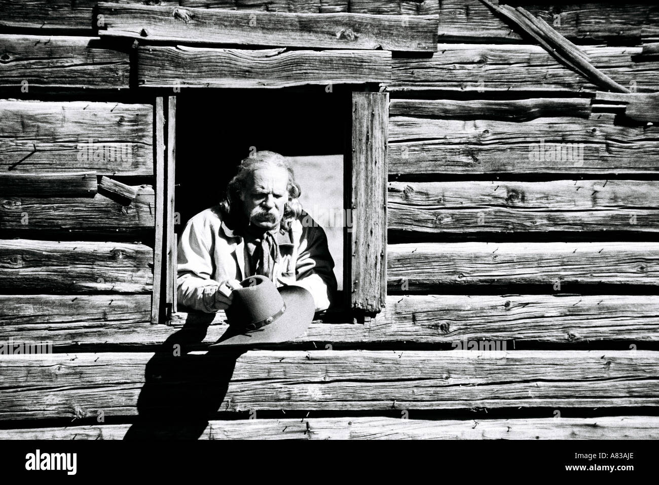 A cowboy in the window of a rustic cabin with his hat off Stock Photo ...