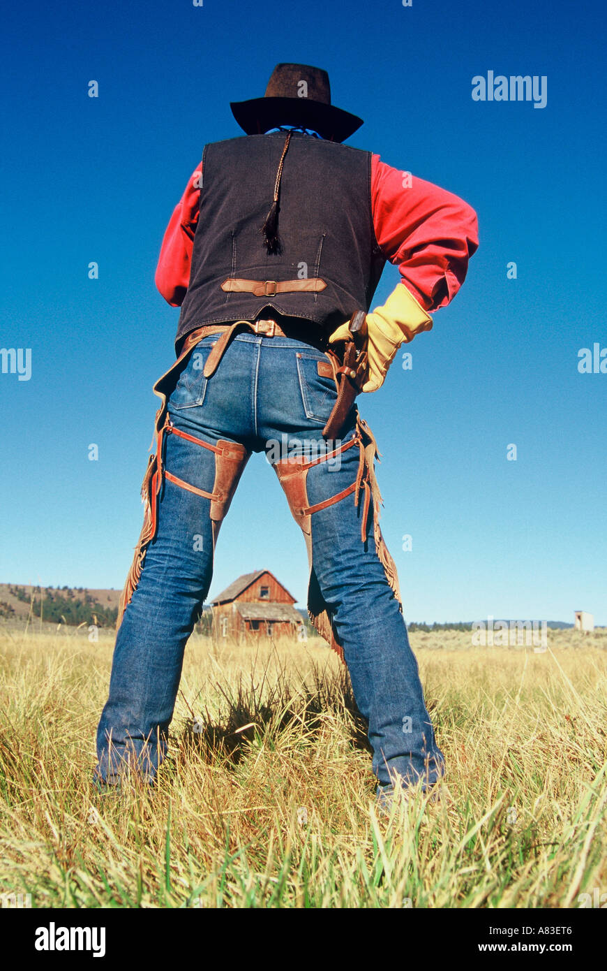 A cowboy standing in front of a homestead cabin ready to draw a firearm ...