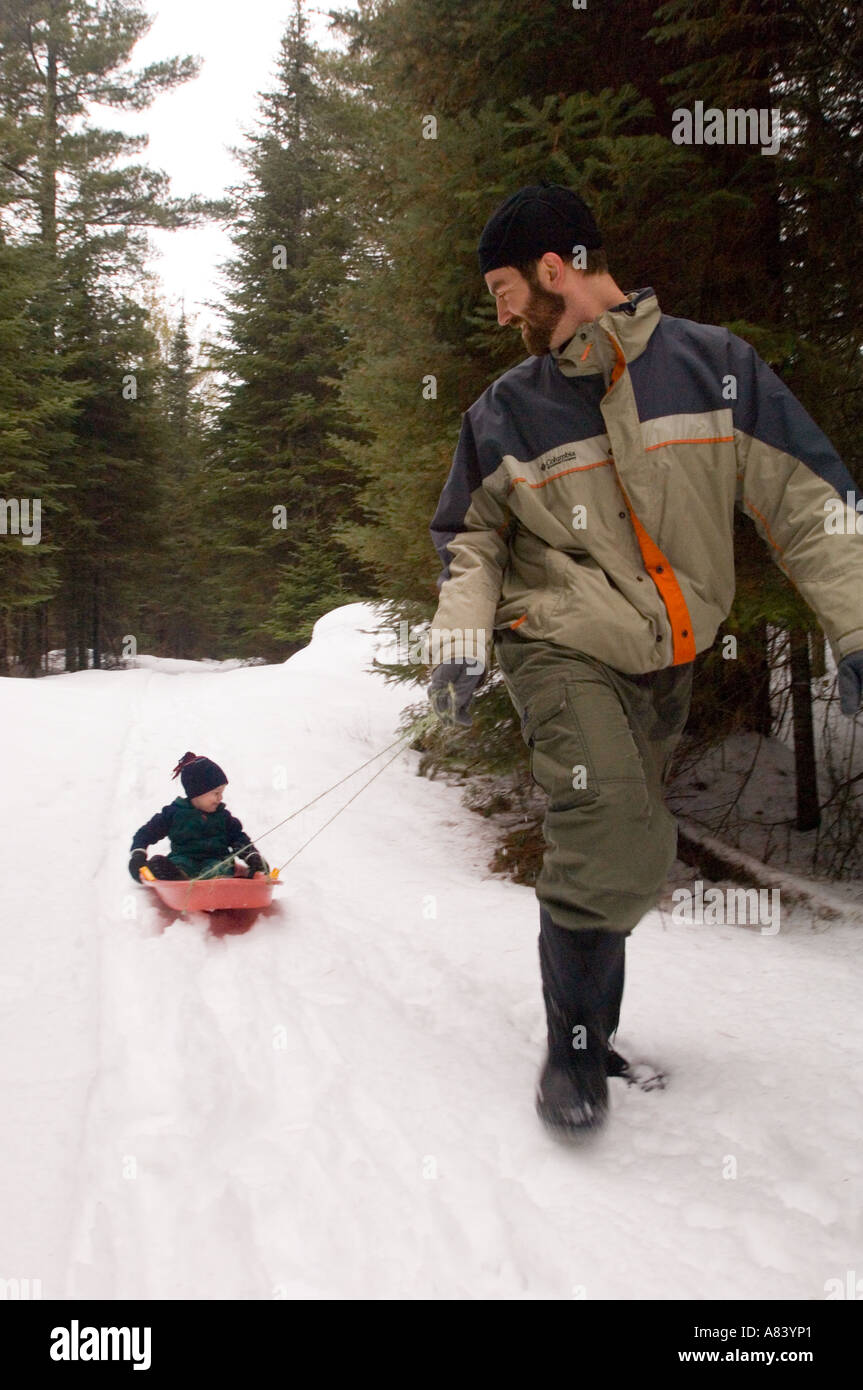 A father pulling his son on sled through the woods Snowshoe Country ...