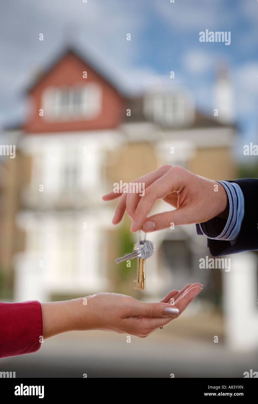 Close up of man's hand passing house keys into woman's hand, house in ...