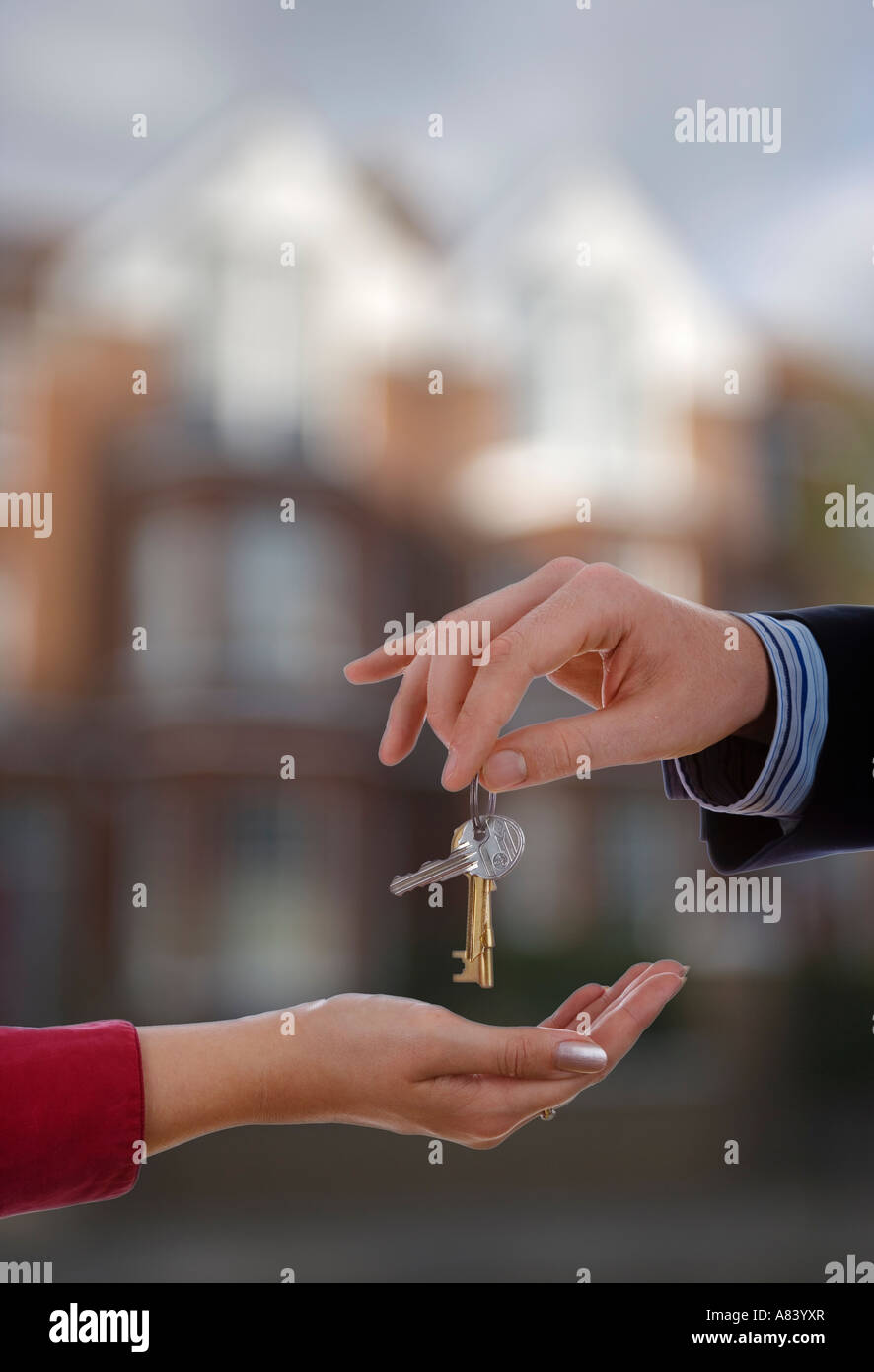 Close up of man's hand passing house keys into woman's hand, house in ...