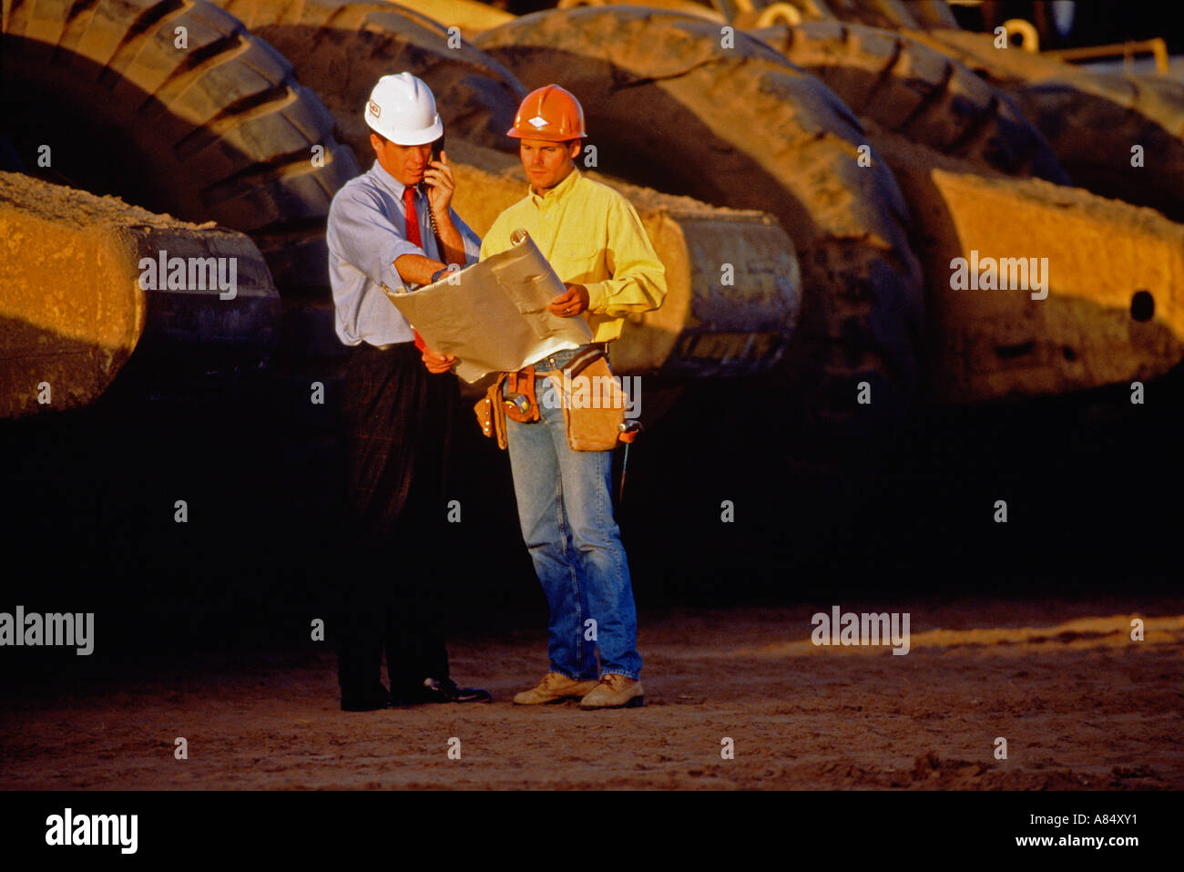 Two men standing outdoors by huge earth moving machine at road ...