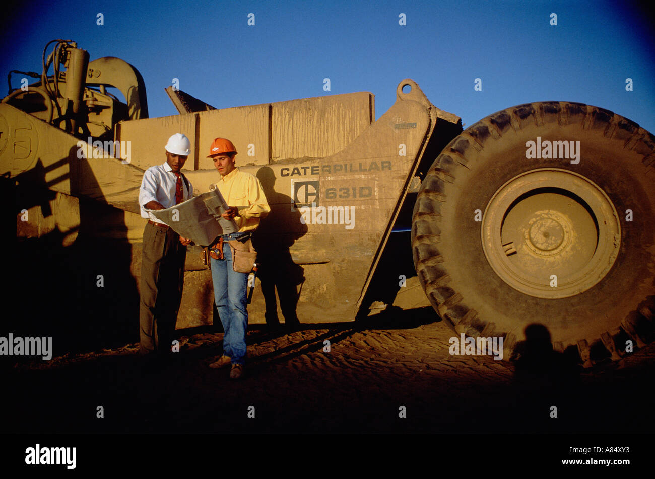 Two men standing outdoors by huge earth moving machine at road ...
