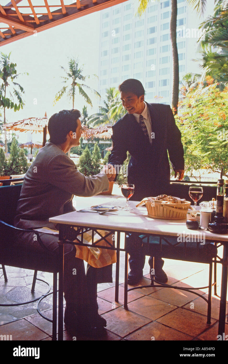 Two men greeting handshake on outdoor terrace of Singapore restaurant ...