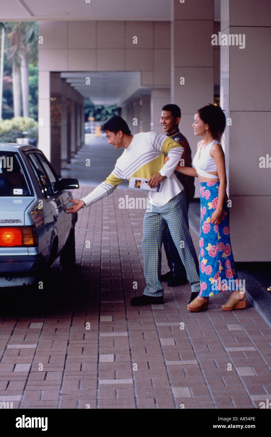Singapore. Young couple by taxi. Man reaching for vehicle door handle ...