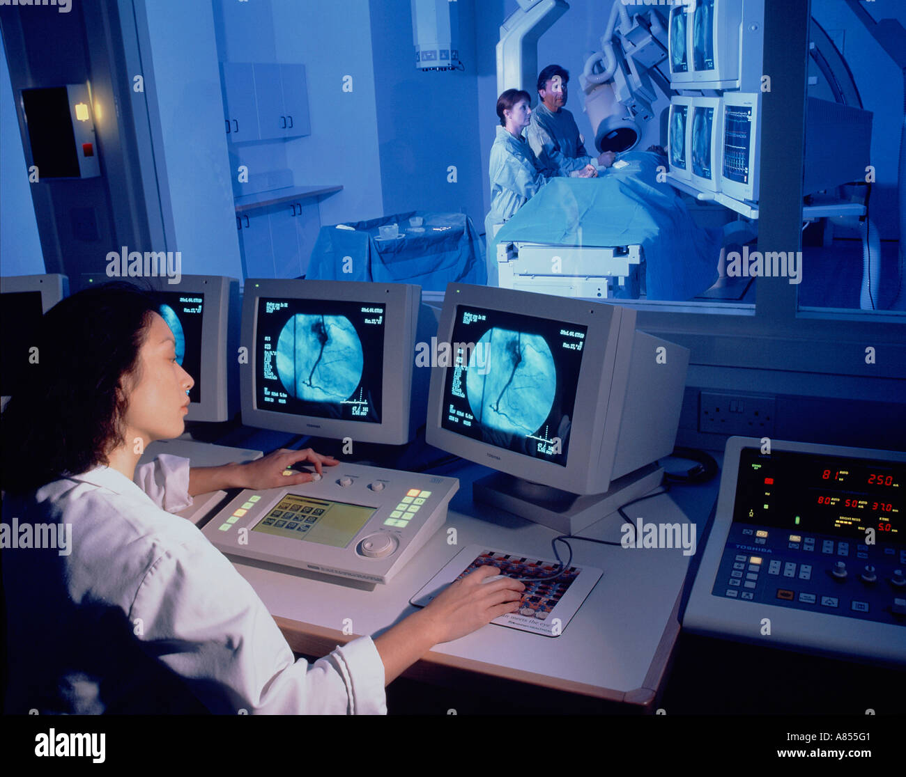 Nurse in computerized control room overlooking surgeon and nurse with ...