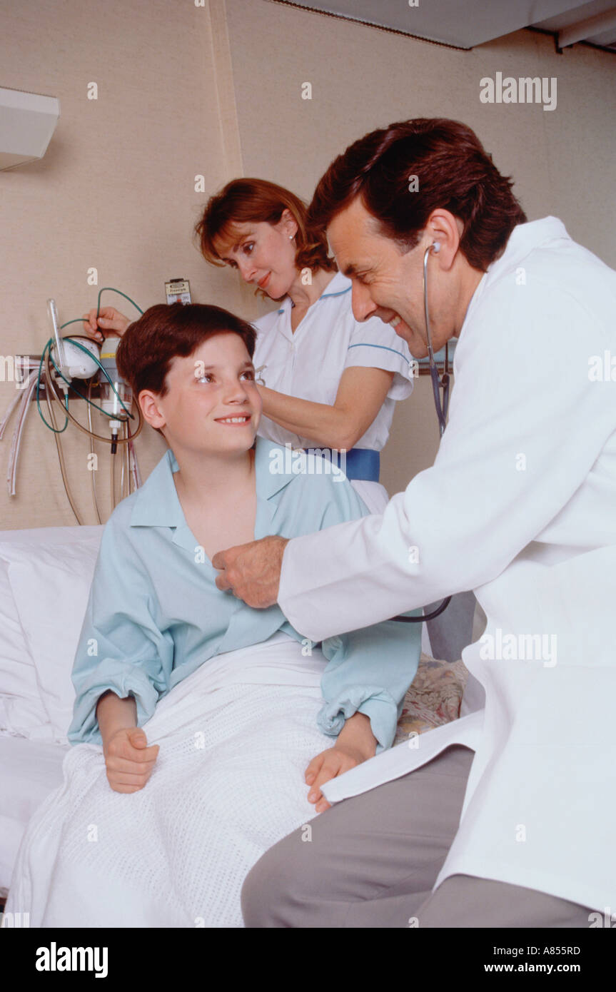 Doctor and nurse tending to young boy patient in hospital bedroom Stock ...