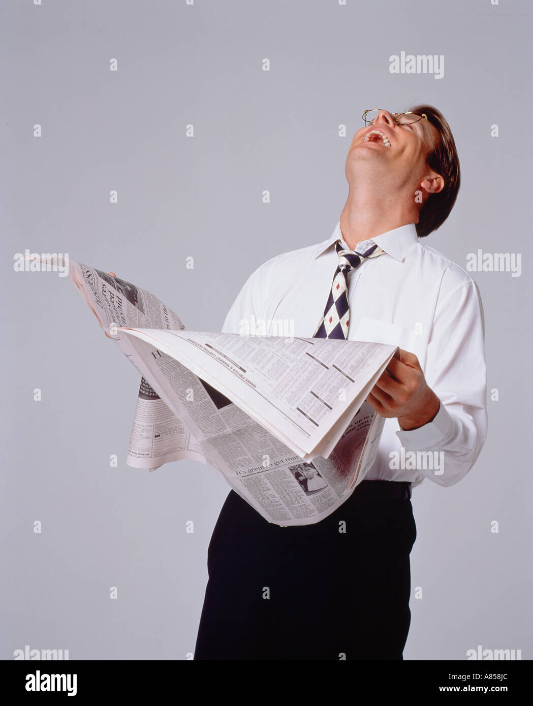Young man in studio reading newspaper and laughing Stock Photo - Alamy
