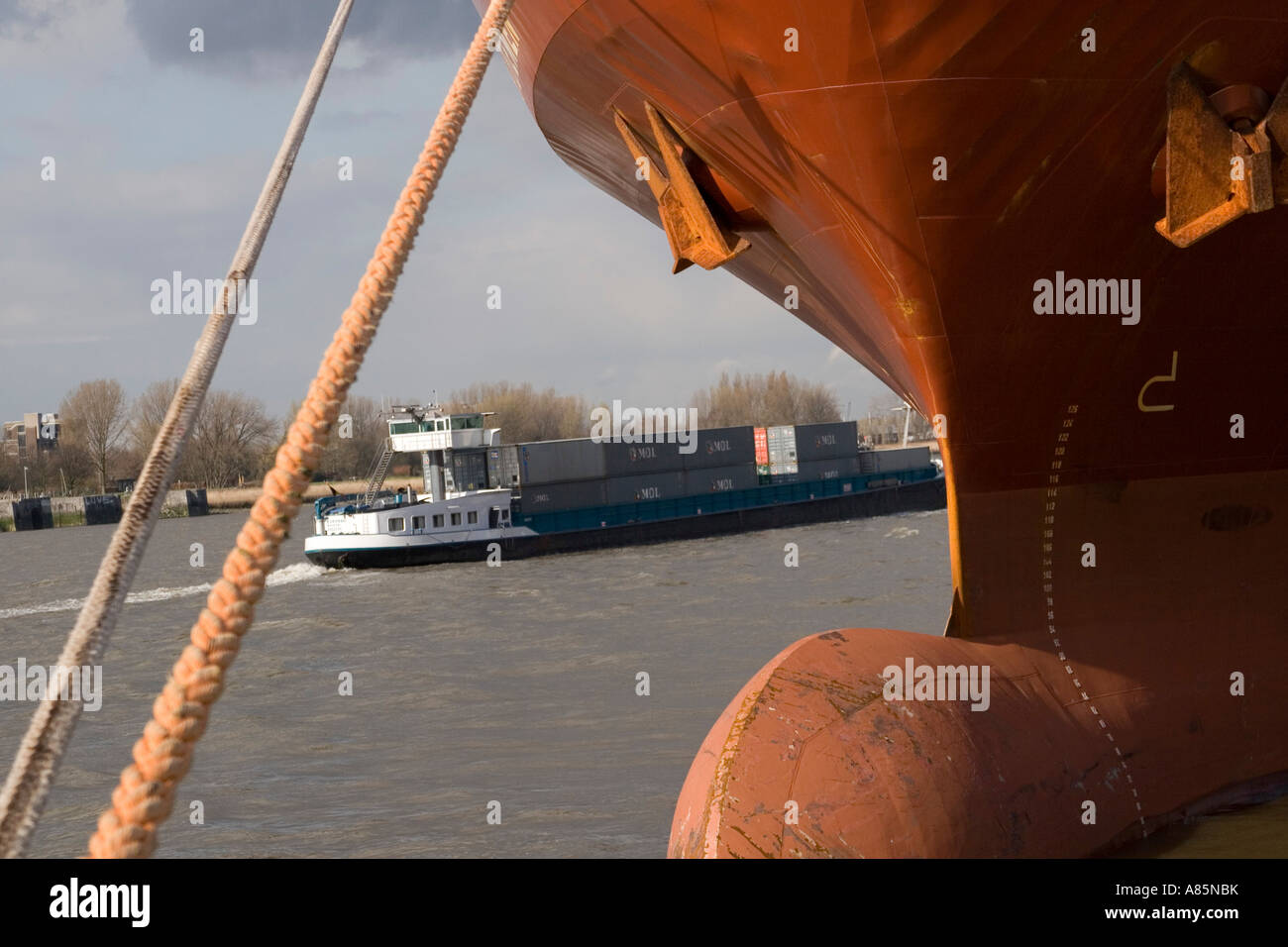 Inland container vessel sailing past moored seagoing container ship ...
