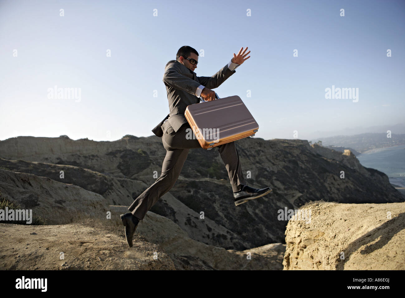 Business man jumping over a cliff holding briefcase Stock Photo - Alamy