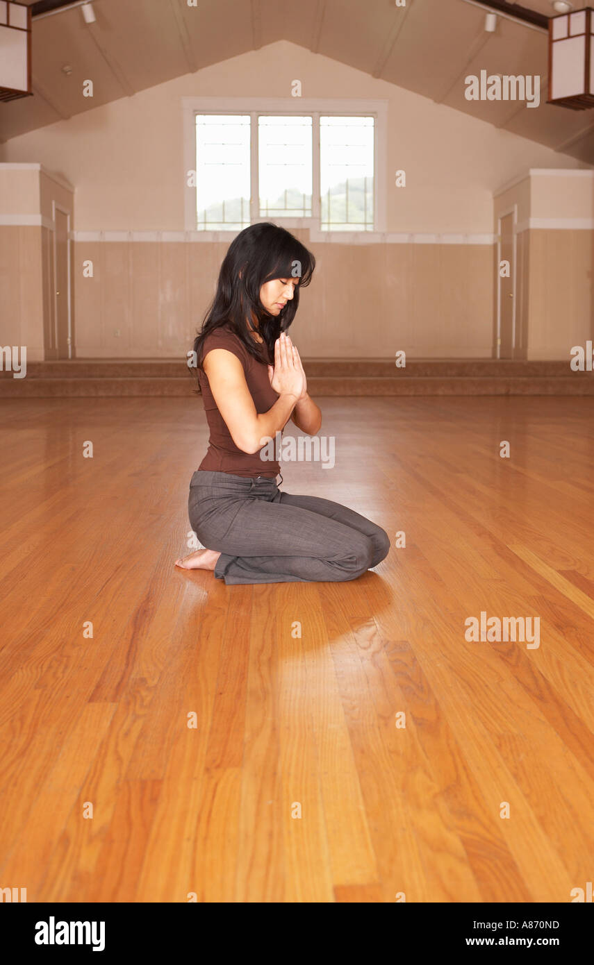 young woman in prayer sitting on the fkloor on her knees in an empty ...