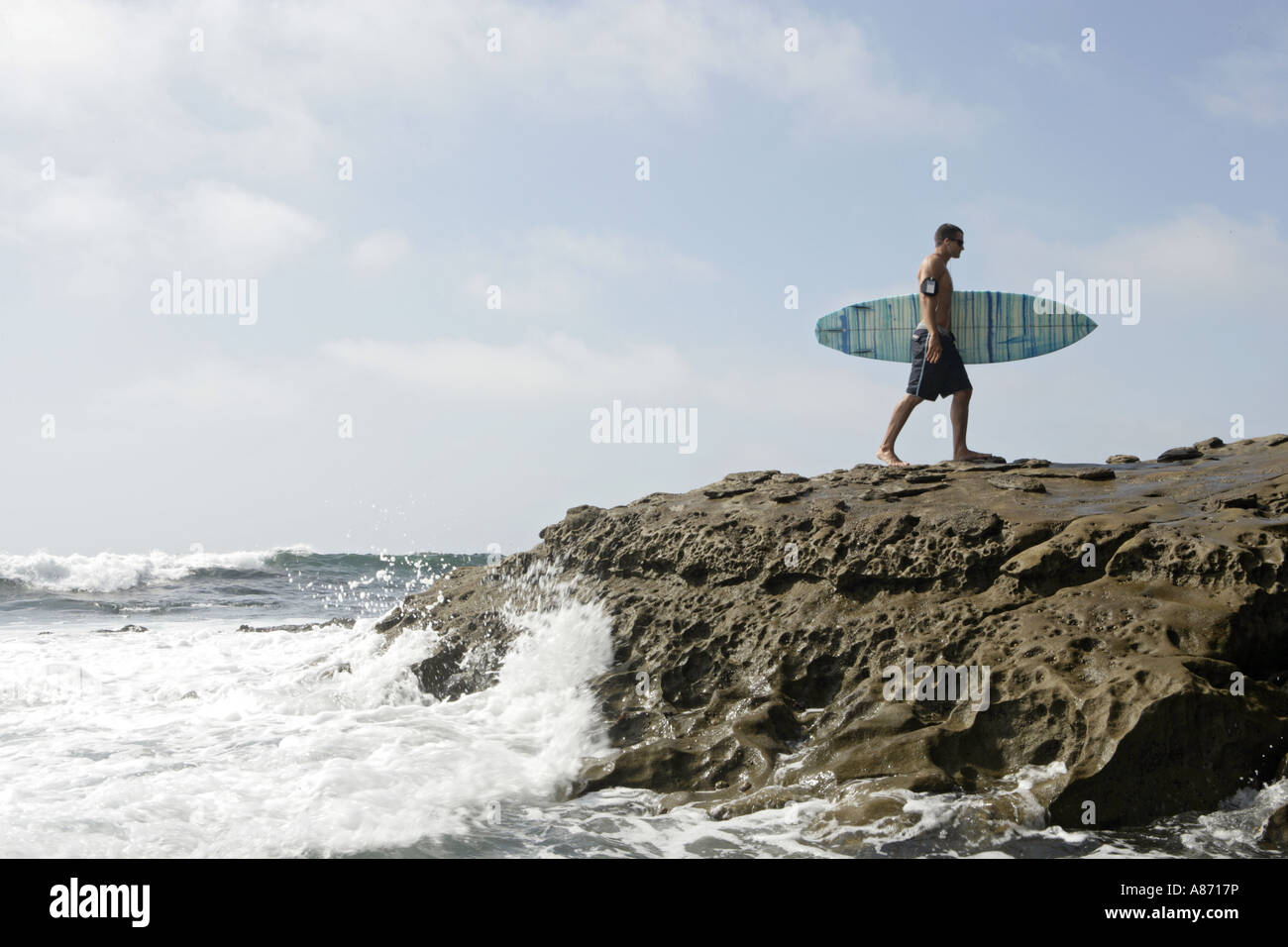 View of a man walking with a surfboard upon a rock Stock Photo - Alamy