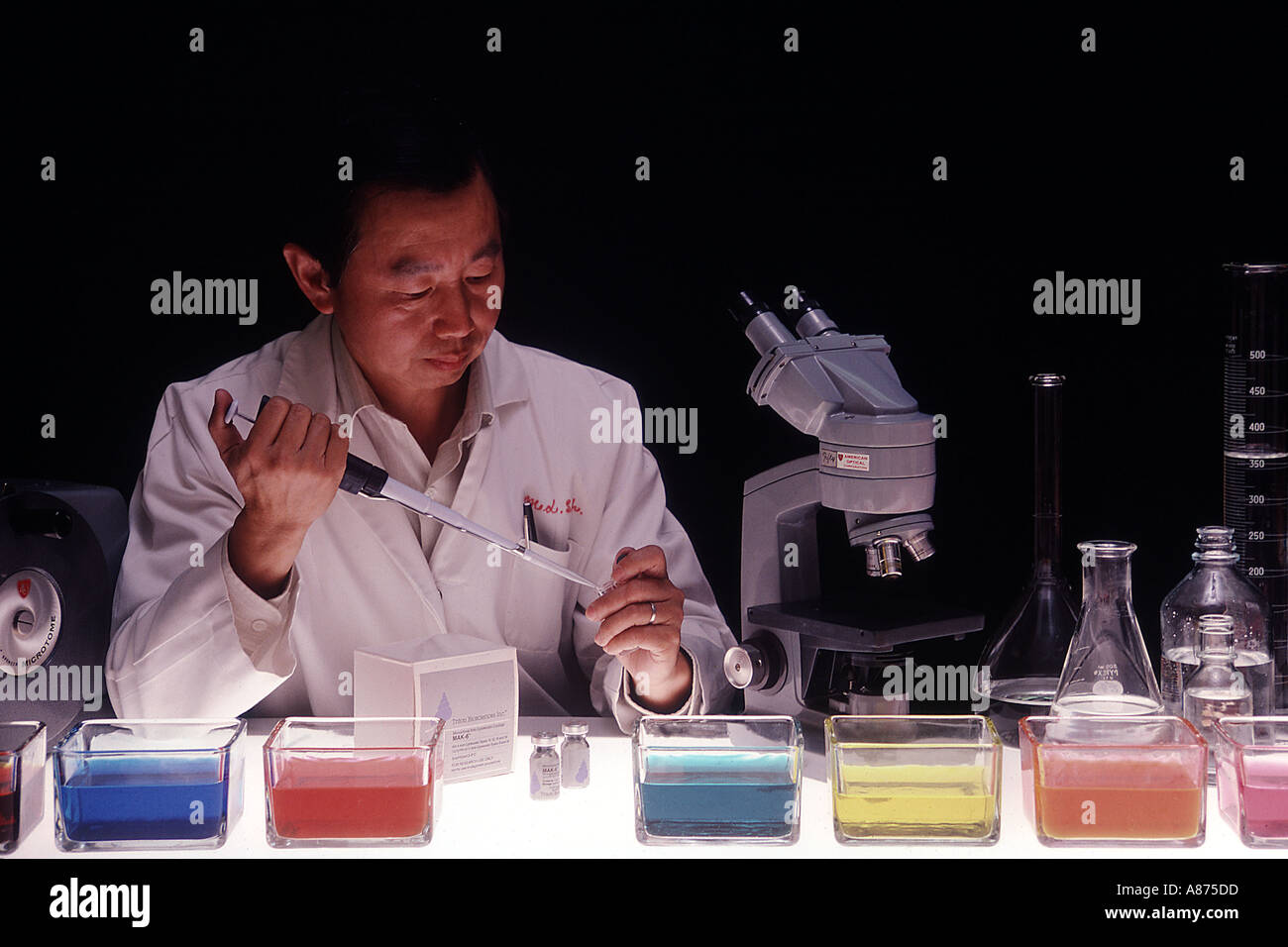 Asian man in laboratory with microscope and vials of colored liquid ...