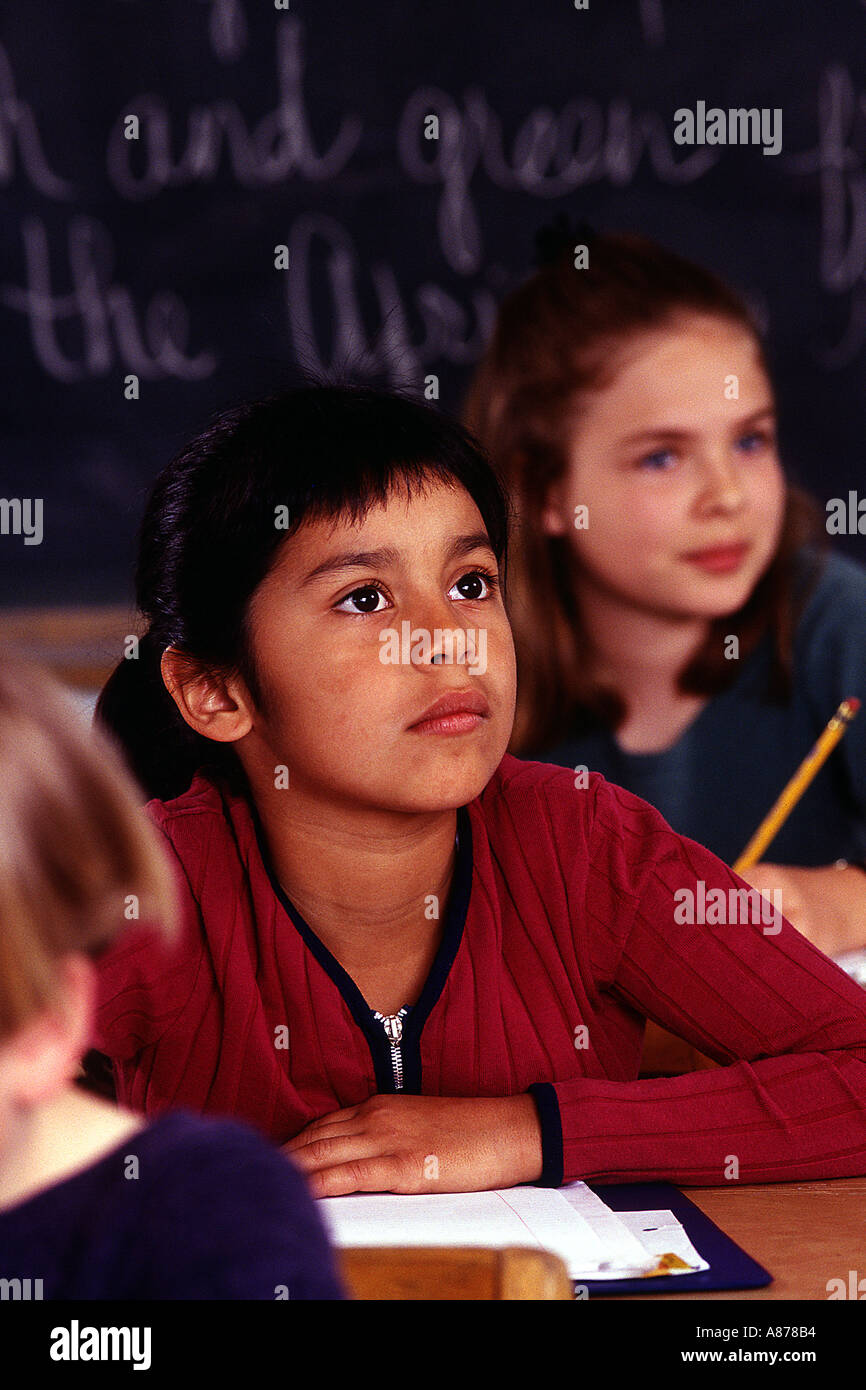 Elementary school children sitting in a classroom listening intently to ...