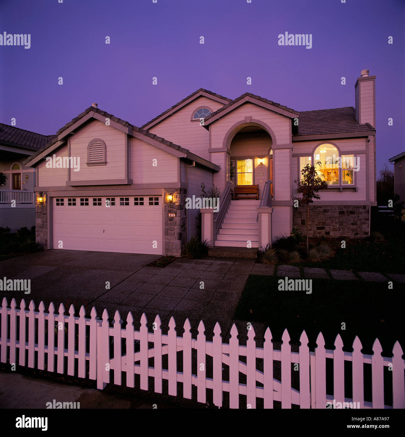 Warm yellow light shines out the windows of a suburban house with a ...