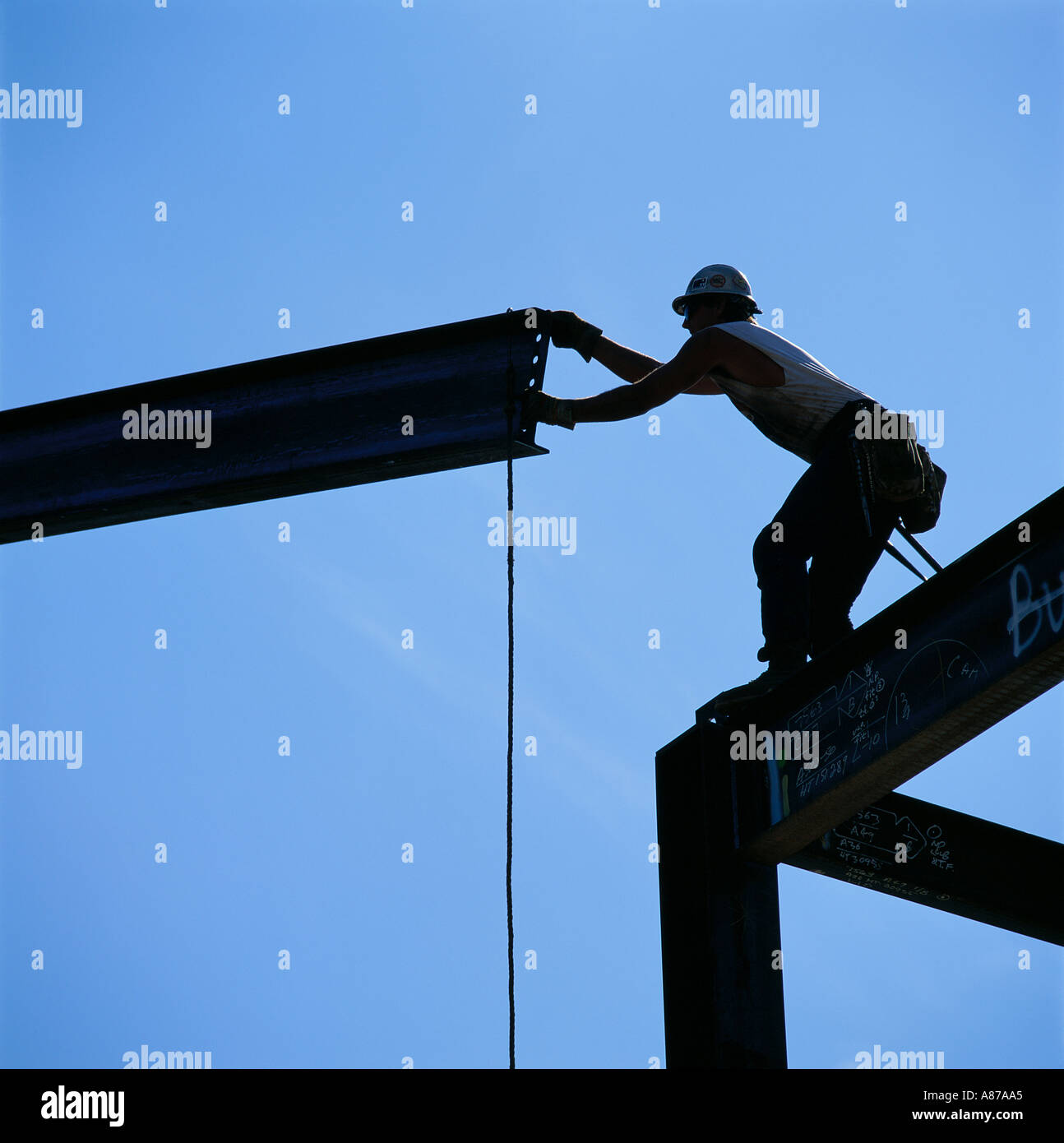 Silhoutted ironworker balancing on steel framework reaches for a girder ...