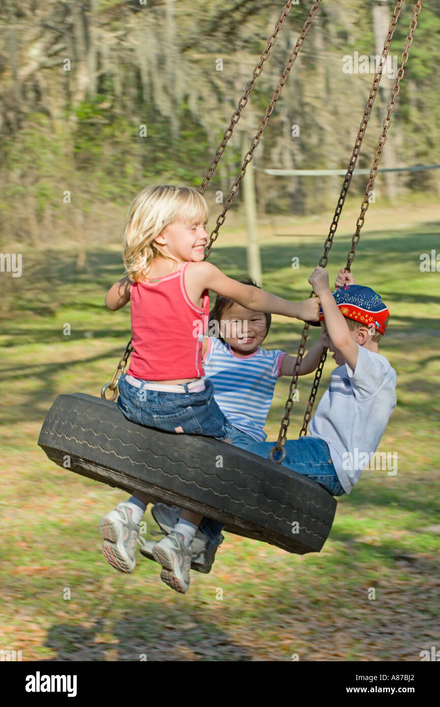 Three young children swinging on a tire swing on a sunny summer day in ...