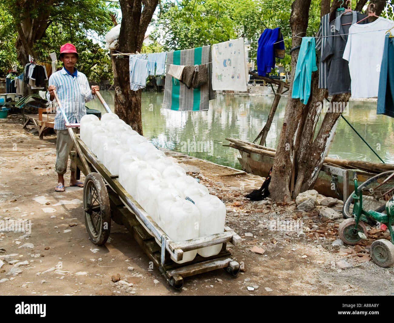 Local man with large trolley of drinking water next to polluted river ...